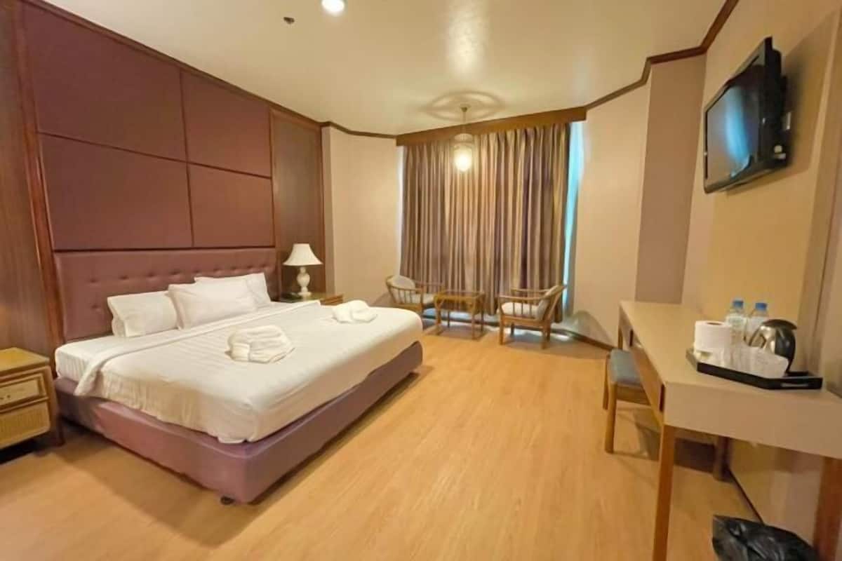 Quarto de hotel com uma cama grande, uma escrivaninha com cadeira, televisão e janela com cortinas.
