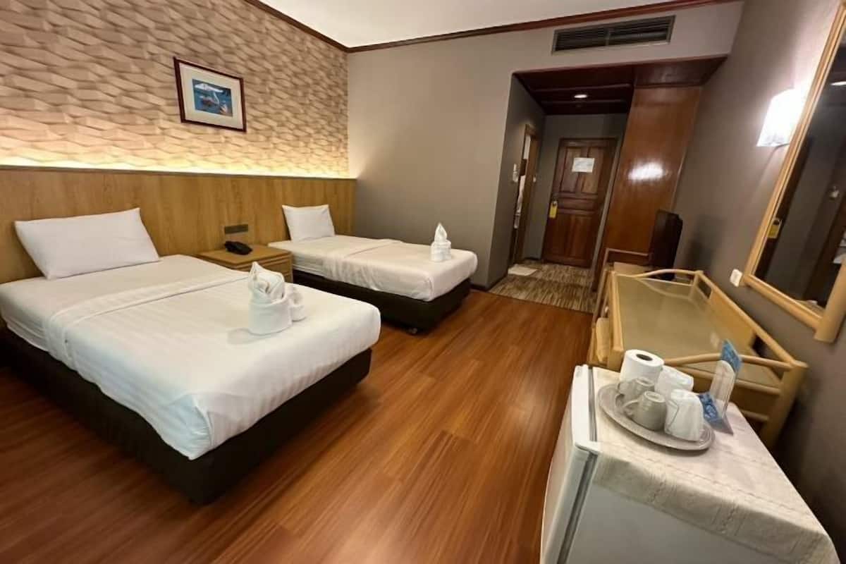 Quarto de hotel com duas camas, piso de madeira, uma mesinha com artigos de higiene pessoal e um espelho.