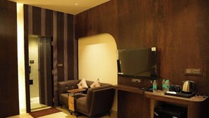Quarto de hotel moderno com sofá, televisão de tela plana, pequeno espaço de cozinha e parede decorativa em madeira.