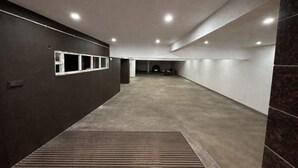 Corredor moderno, com pouca luz, chão de concreto e uma grade de metal na entrada, com uma motocicleta estacionada ao fundo.