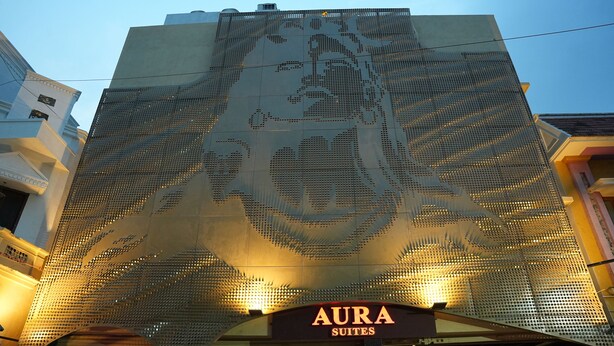Um edifício com uma grande instalação de arte iluminada na parede e a placa 'AURA SUITES' abaixo.