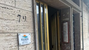 Entrada de um edifício com um letreiro indicando 'ELIOS ROOMS' e o número '79' na parede.