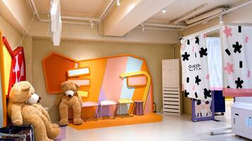 Uma área de recreação infantil com mobiliário colorido, um grande urso de pelúcia e um armário branco.
