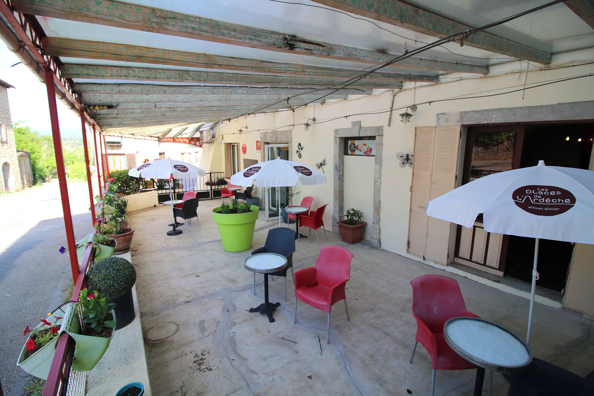 Uma área de café ao ar livre com mesas, cadeiras, guarda-sóis e plantas em vasos.