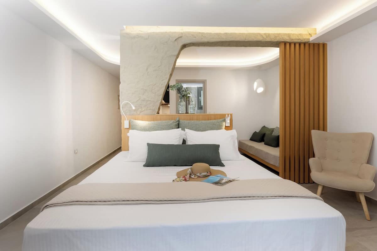 Quarto de hotel moderno com uma cama, uma cadeira, uma mesa de cabeceira e um espelho.