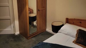 Quarto com cama, guarda-roupa de madeira, mesa de cabeceira redonda e espelho.