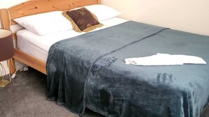 Uma cama de solteiro com cabeceira de madeira, colcha verde escura e almofada estampada.