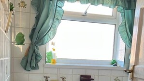 Um banheiro pequeno com pia branca, janela com cortinas e piso estampado.