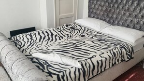 Quarto com cama, cabeceira estofada cinza, porta branca e tapete estampado.