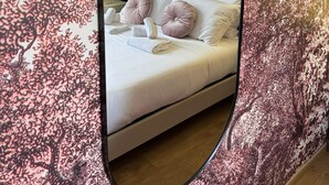 Quarto com cama, almofadas e espelho fixado na parede.