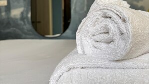 Toalha branca dobrada sobre a cama, com um mural de árvores na parede e um espelho refletindo uma porta.