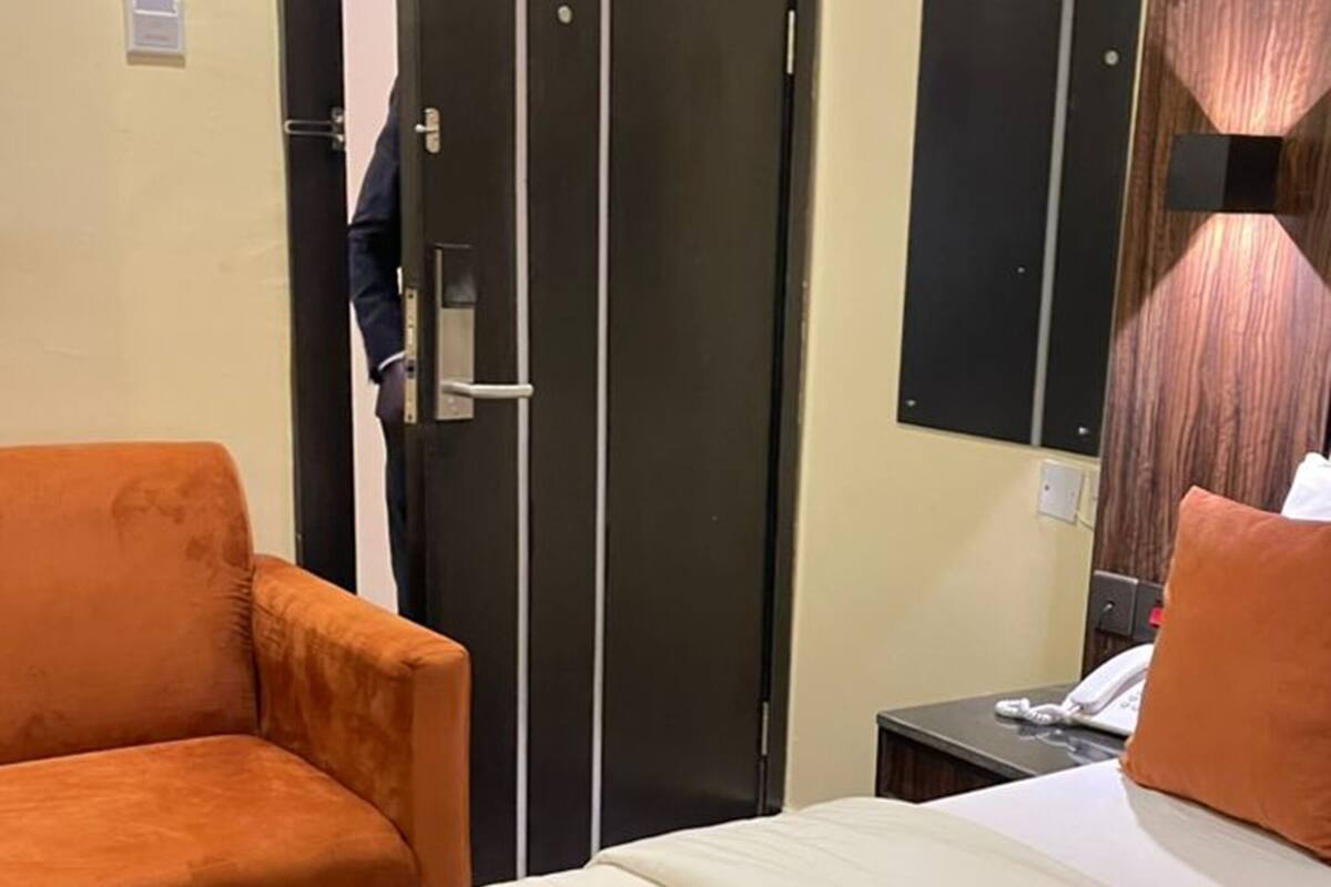 Quarto de hotel com cama, uma cadeira, escrivaninha com luminária e espelho.