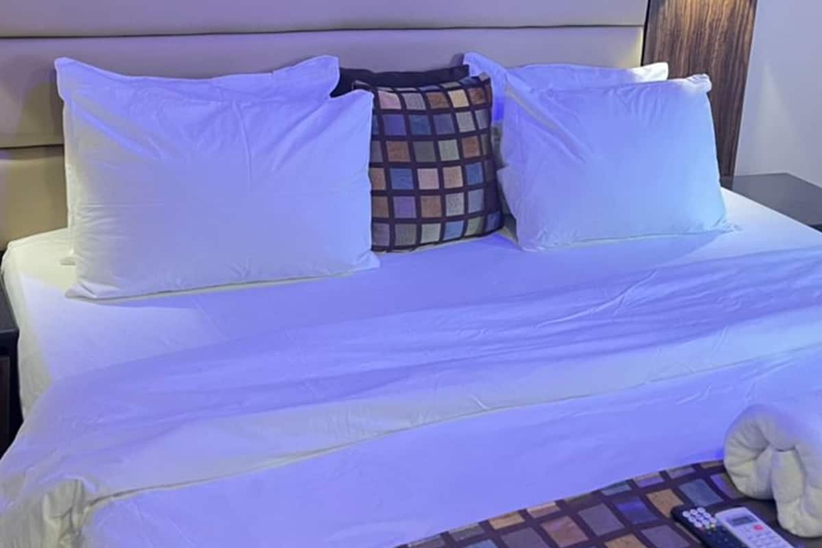 Quarto de hotel com uma cama grande, cabeceira com luminária e controle remoto na mesa de cabeceira.