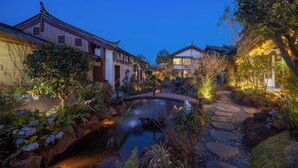Um pátio tradicional com um pequeno lago, ponte de pedra e edifícios com arquitetura clássica.