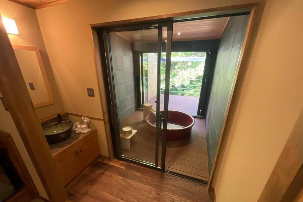 Casa de banho com toucador de madeira, lavatório e sanita. Porta de vidro dá para uma varanda com banheira de hidromassagem.
