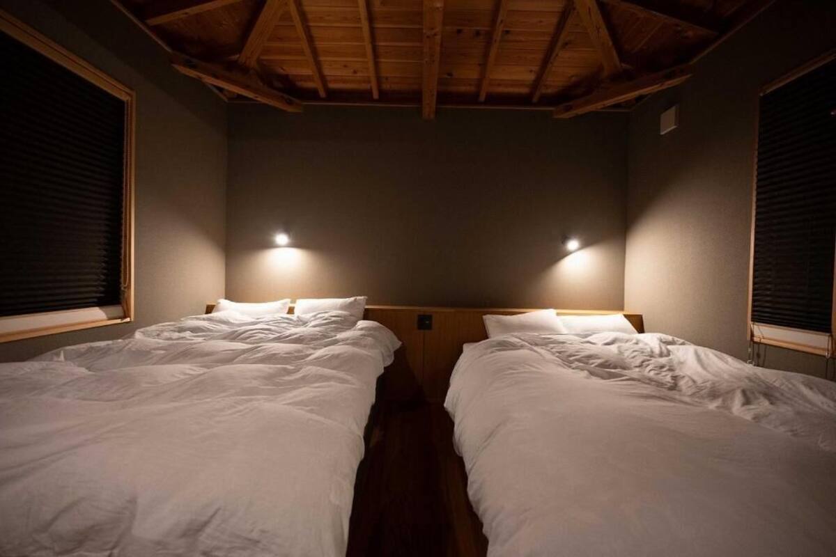 Quarto com duas camas, vigas de madeira no teto e luminárias fixadas na parede.