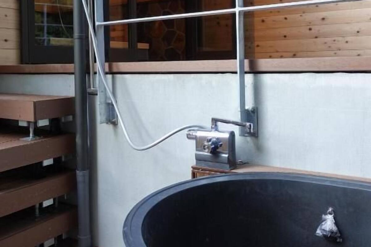 Uma cabana de madeira com uma banheira preta grande, uma escada de metal e uma janela com vista para o interior.