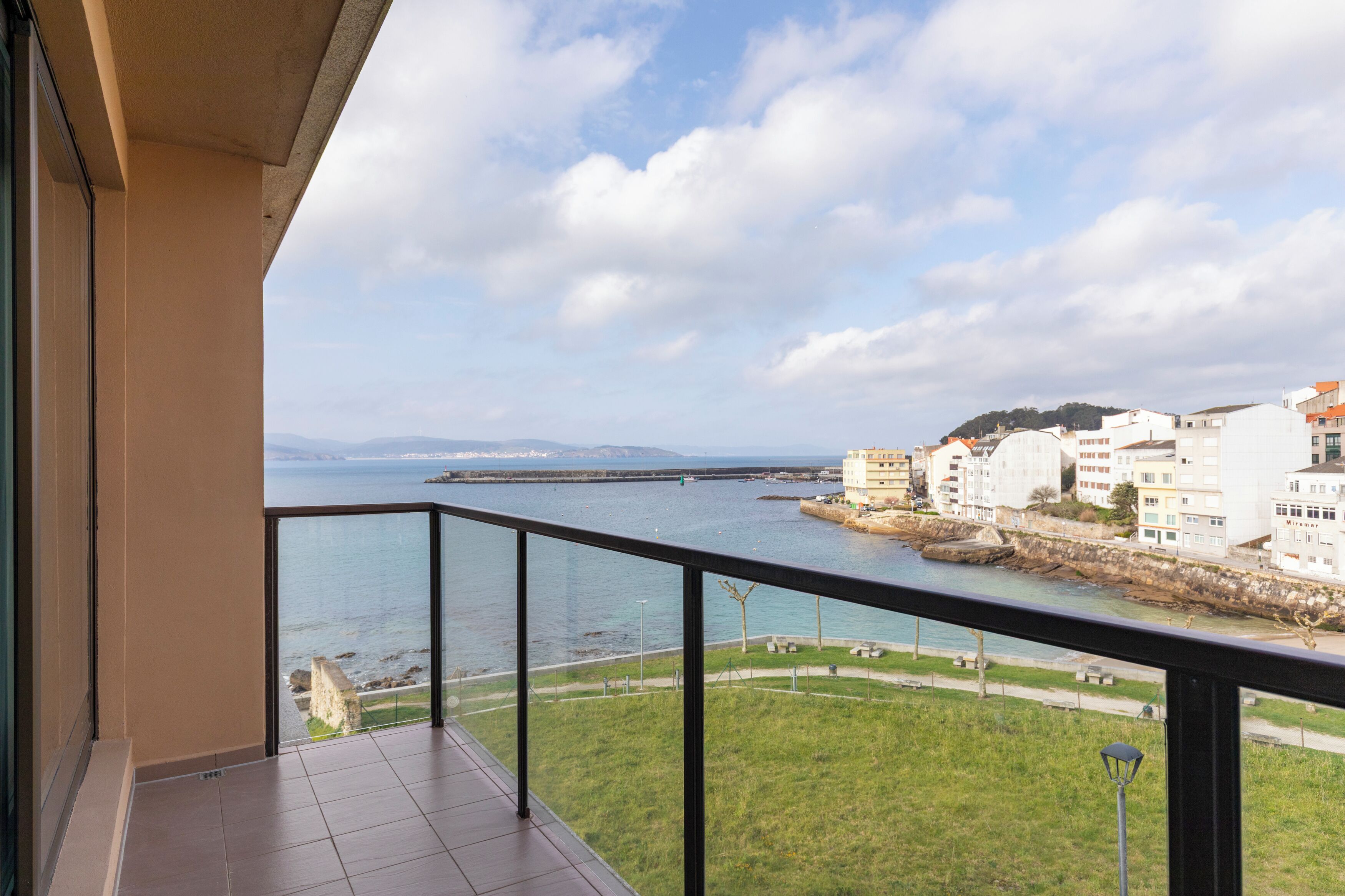 Uma varanda com vista para o mar, edifícios e uma cadeia montanhosa ao longe.