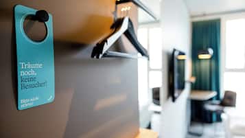 Um letreiro cor de verde-água com texto em língua estrangeira, um cabide preto e uma vista desfocada do interior de um quarto com uma mesa e cadeiras.