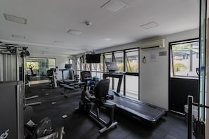 Uma academia com equipamentos de cardio, aparelhos de musculação e uma grande janela com vista para o exterior.