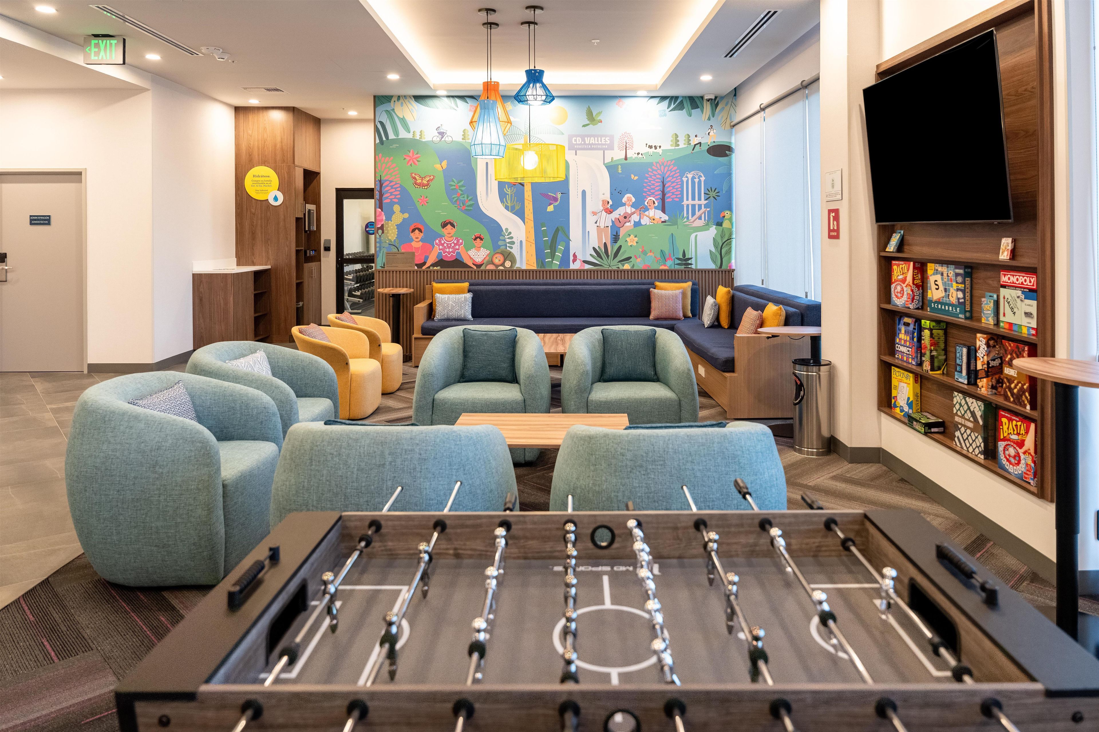 Uma área de estar moderna com mesa de pebolim, assentos confortáveis e um mural na parede.