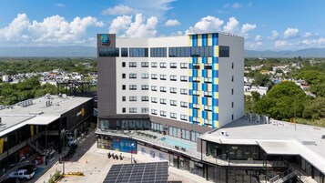 Um hotel moderno com piscina no terraço, vários andares e vista para a paisagem urbana ao redor.