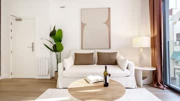 Sala de estar moderna com sofá branco, mesa de centro redonda de madeira, planta em vaso e uma grande pintura abstrata na parede.