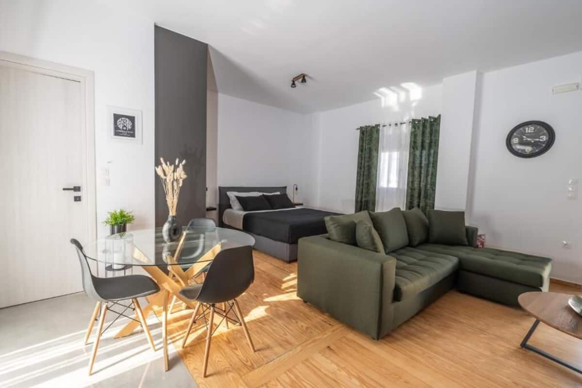 Uma sala de estar moderna com uma mesa de jantar de vidro, um sofá verde, uma cama e um relógio na parede.