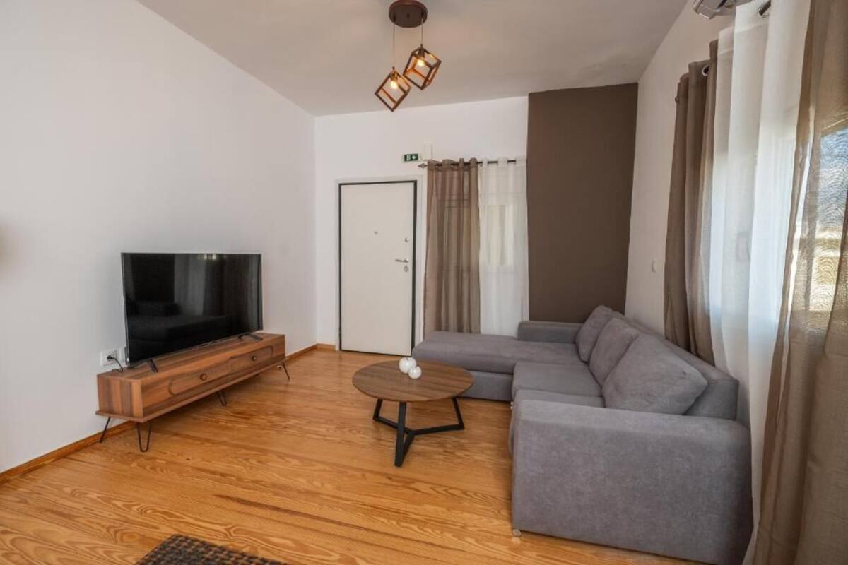 Uma sala de estar moderna com uma televisão de tela plana, um móvel para TV de madeira, um sofá cinza, uma mesa de centro redonda e um lustre.