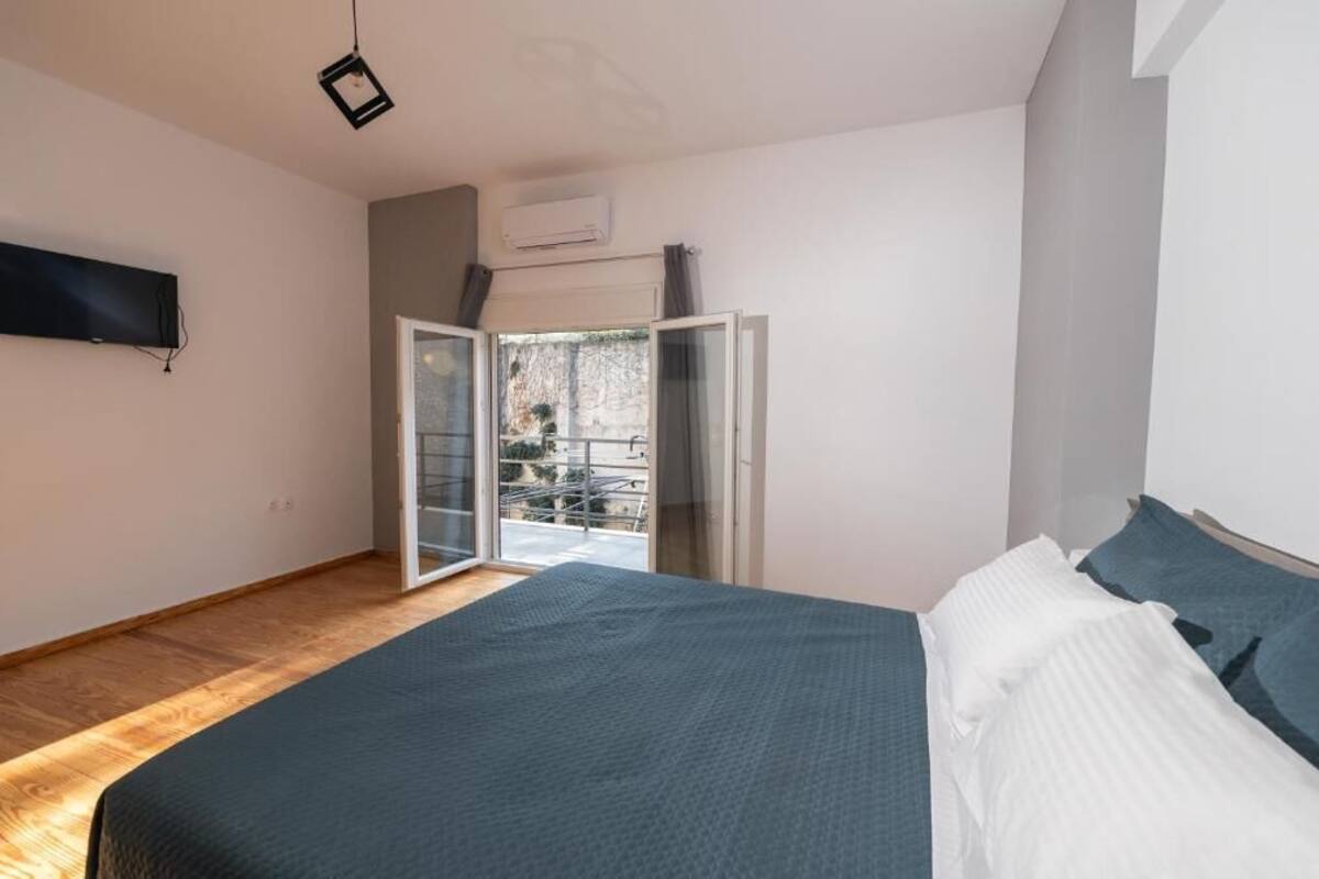 Quarto com cama, televisão, ar condicionado e porta aberta para uma varanda.