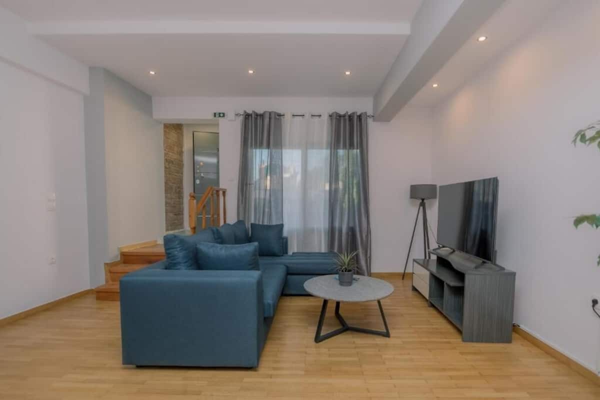 Uma sala de estar moderna com sofá seccional, mesa de centro redonda, TV em um suporte e escada para um andar superior.