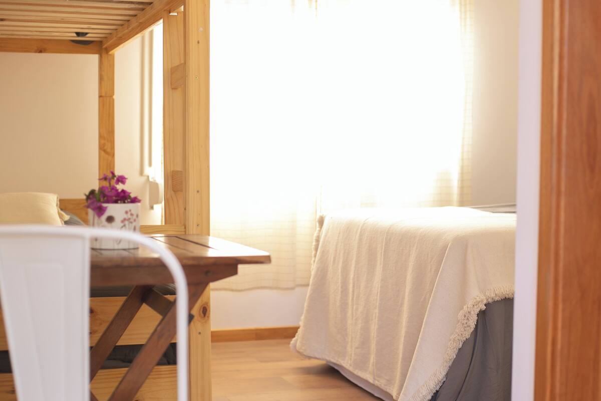 Um quarto com uma cama, uma mesa com um vaso de flores e uma cadeira.