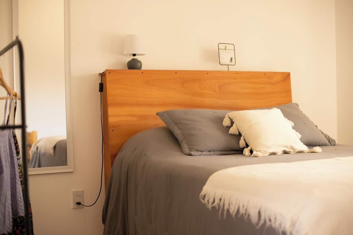 Uma cama bem arrumada com cabeceira de madeira, luminária de cabeceira e interruptor de luz na parede.