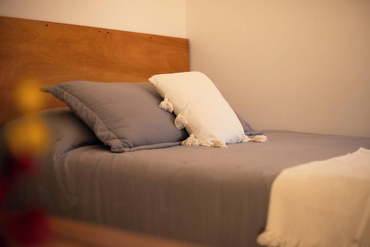 Cama com cabeceira de madeira, dois travesseiros e um cobertor.