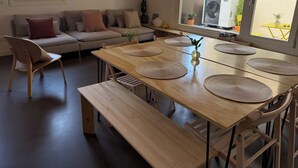 Um espaço de estar moderno com uma mesa de jantar de madeira, bancos e um sofá com almofadas.