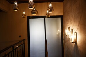 Uma escadaria com corrimão, uma porta de vidro jateado e luminárias fixadas na parede.