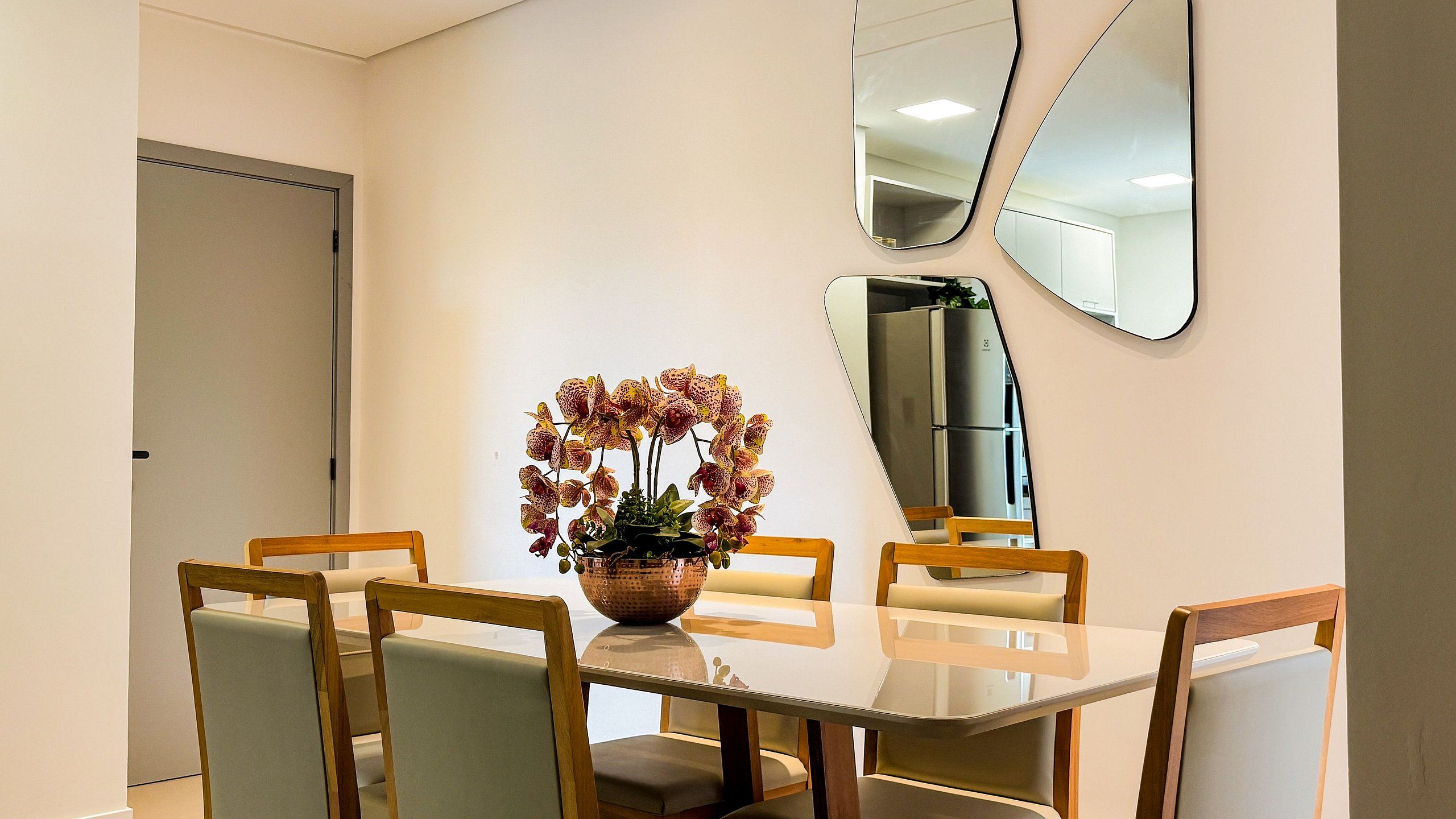 Sala de conferências com mesa, cadeiras, uma orquídea em vaso e espelhos na parede.