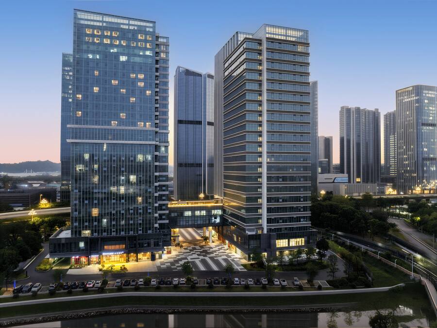 Um edifício moderno com fachada de vidro, entrada central e área de estacionamento.