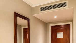 Um corredor com piso de madeira, uma porta de madeira com fechadura e um respiradouro no teto.