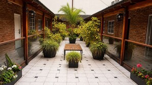 Um pátio com um banco de madeira central, rodeado por plantas em vasos e um chão de azulejos.