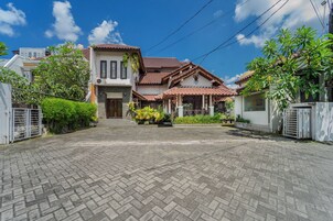 Uma casa de dois andares com telhado ladrilhado, varanda frontal e entrada de automóveis pavimentada.