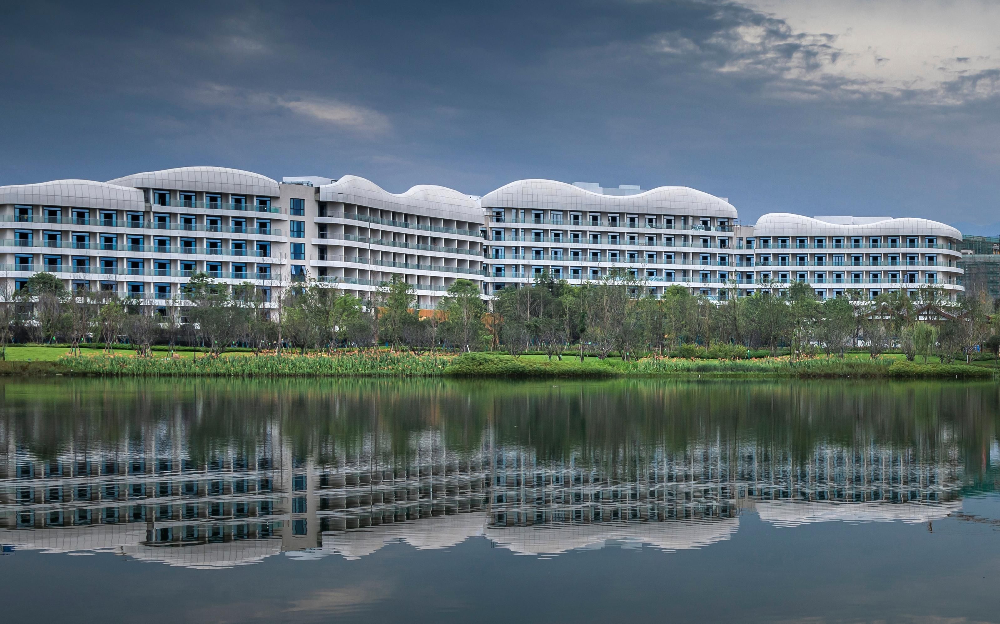 Um hotel moderno com vários andares, grandes janelas e um reflexo na água.