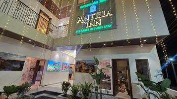 Um átrio de hotel com uma placa indicando 'ANTILLA INN', várias varandas, plantas em vasos e obras de arte nas paredes.