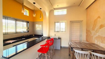 Uma cozinha com bancada preta, banquetas vermelhas e uma mesa de jantar com cadeiras brancas.