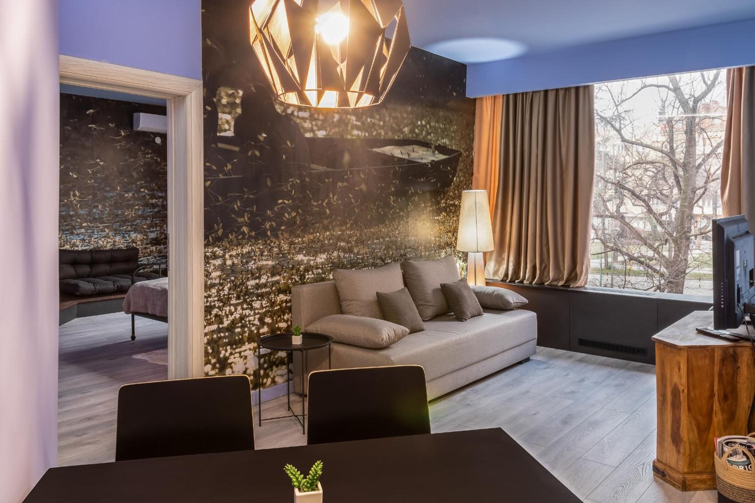 Uma sala de estar moderna com sofá, mesa de jantar, TV e uma janela grande com cortinas.