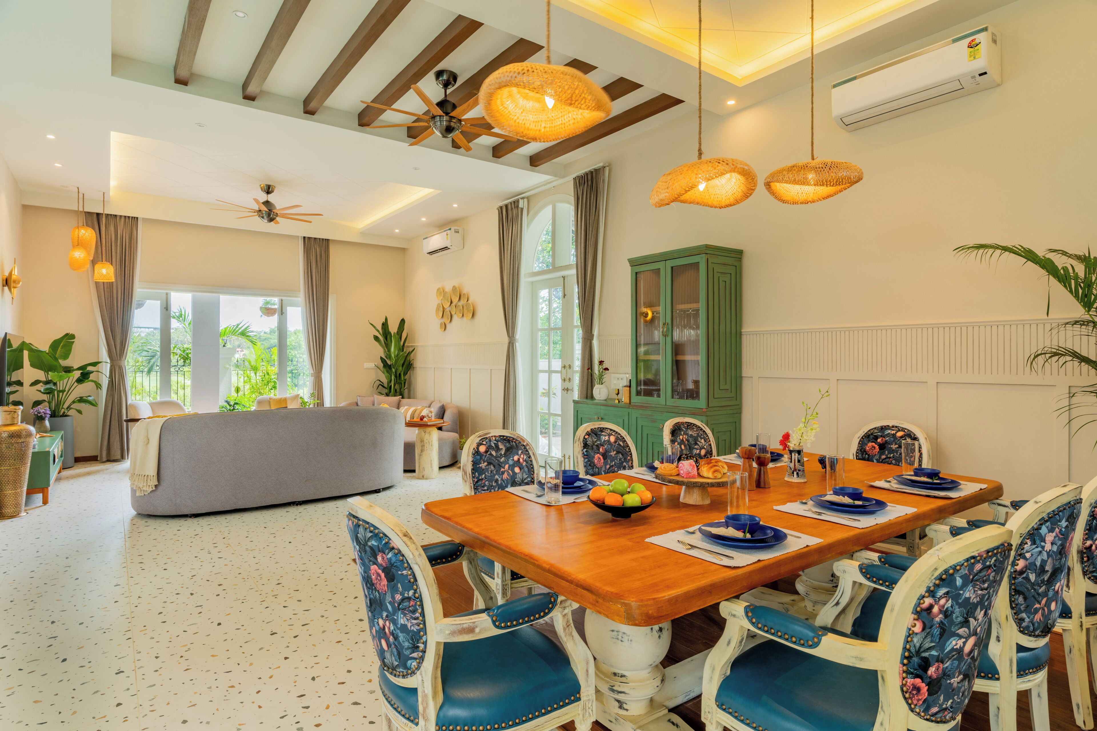 Uma sala de jantar com uma mesa de madeira, cadeiras estofadas em azul e luminárias de vime suspensas.
