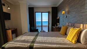 Quarto de hotel com uma cama grande, uma escrivaninha, uma cadeira, uma televisão e vista para o oceano pela porta.
