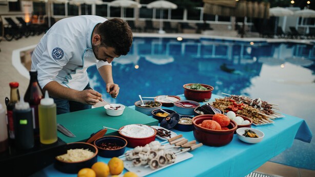 Buffet junto à piscina, com diversos alimentos e um atendente.