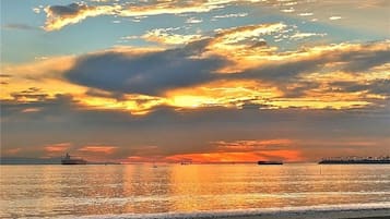 Um pôr do sol sobre um mar calmo com navios ao longe.