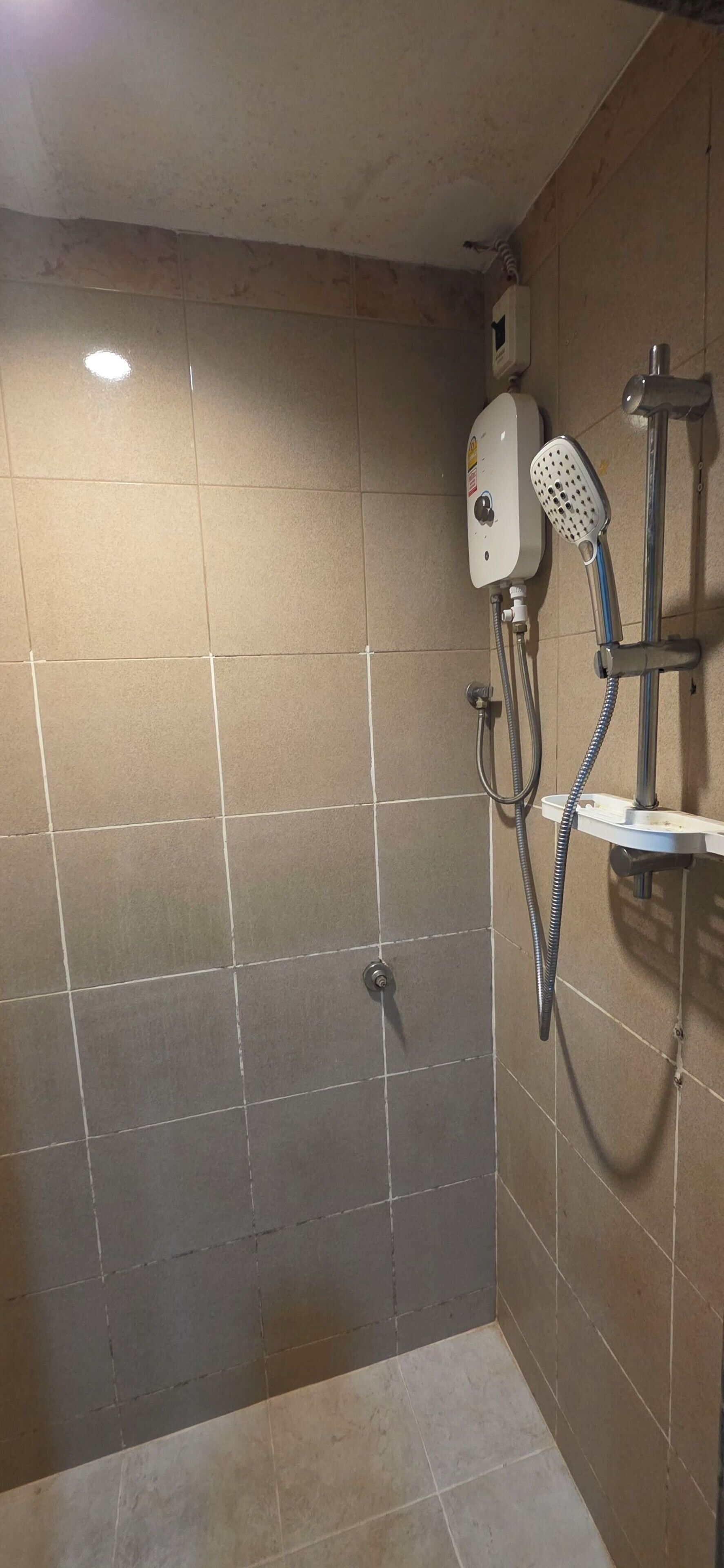 Área de duche com chuveiro manual, torneira embutida e painel de controlo.